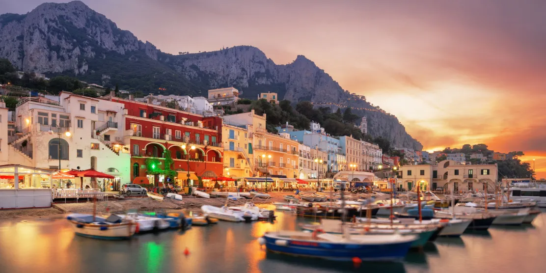 Harbor at sunset with boats and mountain cliffs in Capri, Italy.