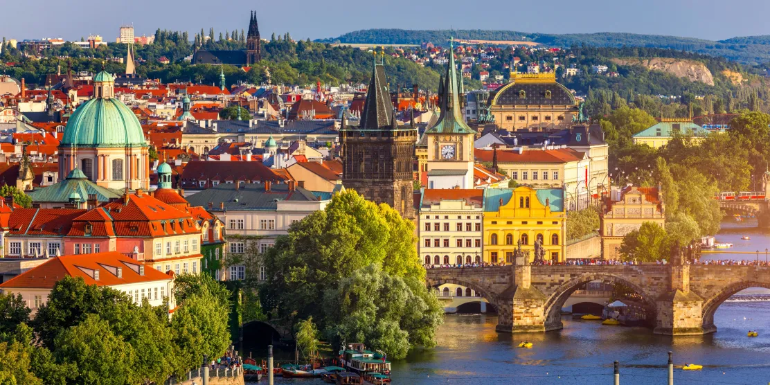 Historic bridges and Gothic spires of the Prague skyline at sunset.