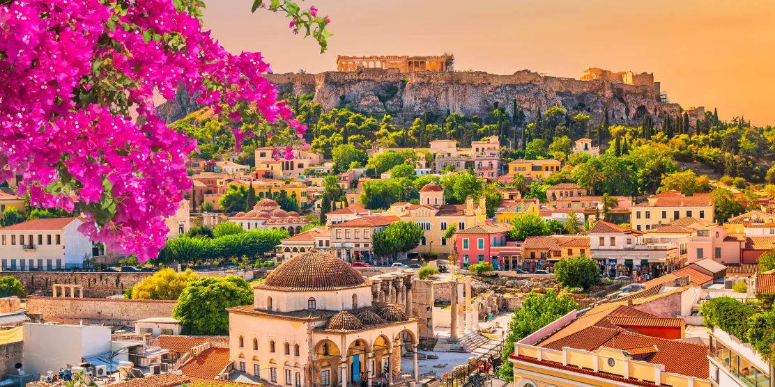 View of the Acropolis and Parthenon in Athens, Greece, seen from below through a branch of vivid pink bougainvillea flowers, overlooking the historic Plaka neighbourhood