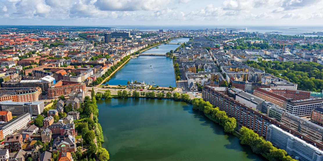 Aerial view of Copenhagen, Denmark, showing the city's lakes (Søerne) lined with trees and historic apartment buildings, with the harbour visible in the distance