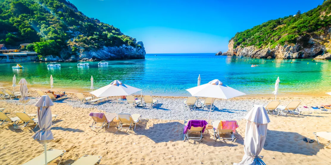 Sunny Greek island beach with turquoise water and lounge chairs under umbrellas
