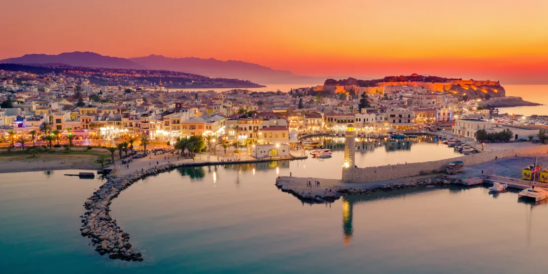 Harbor town in Greece at sunset with illuminated waterfront buildings