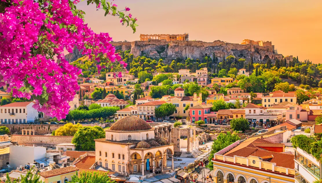 View of the Acropolis and Parthenon in Athens, Greece, seen from below through a branch of vivid pink bougainvillea flowers, overlooking the historic Plaka neighbourhood