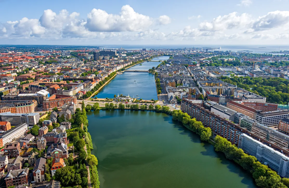 Aerial view of Copenhagen, Denmark, showing the city's lakes (Søerne) lined with trees and historic apartment buildings, with the harbour visible in the distance