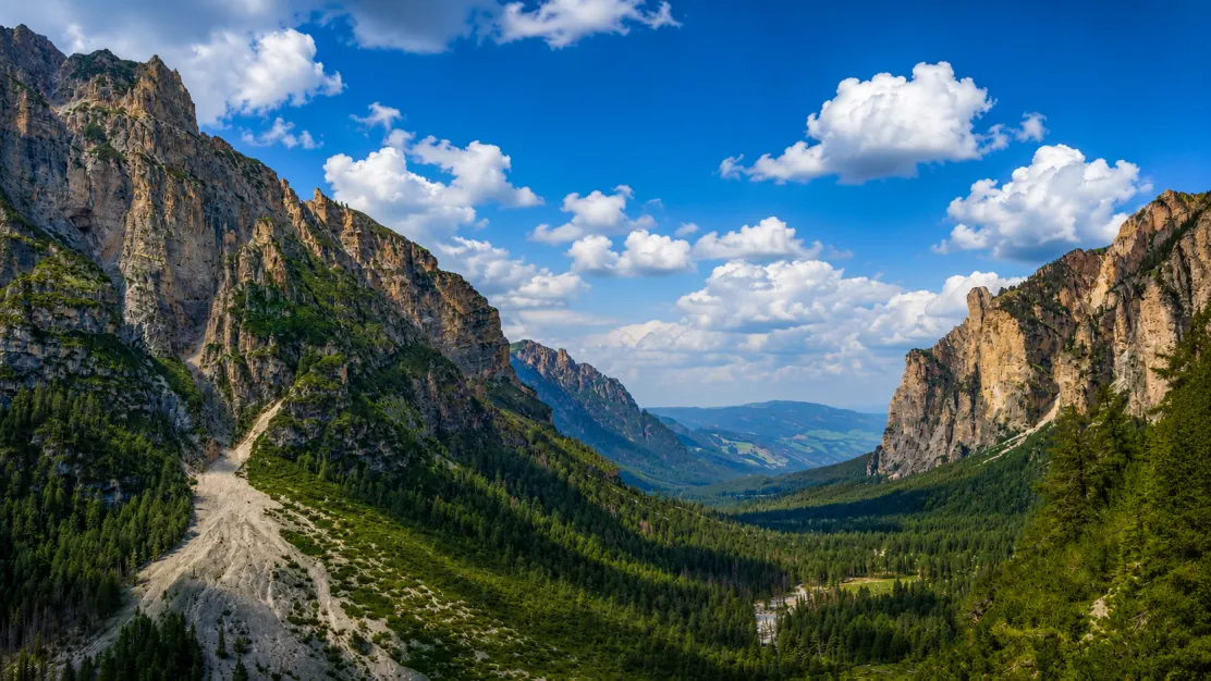 Dolomites Alta Via 1 hiking trail winding through a lush green valley enclosed by dramatic rocky peaks in Italy.