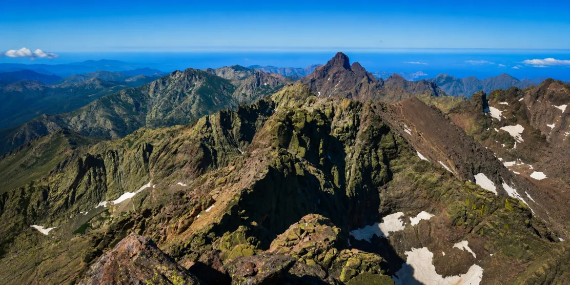 GR20 hiking trail showcasing rugged, sharp mountain ridges with patches of snow under a clear blue sky in Corsica.
