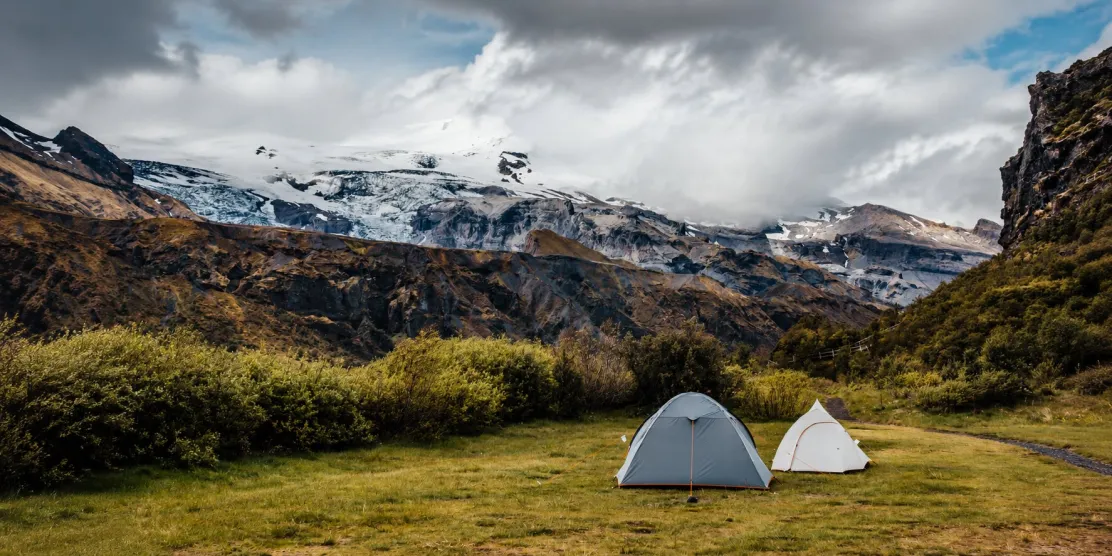 Laugavegur Trail showing camping tents pitched on a green meadow facing massive glaciers and volcanic mountains.