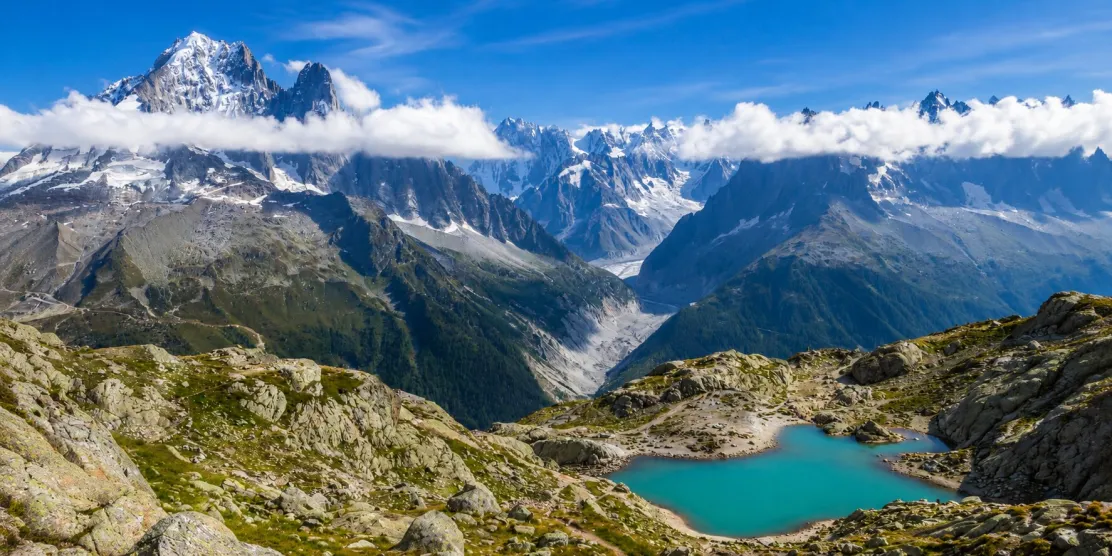Tour du Mont Blanc hiking trail with a vibrant turquoise alpine lake in the foreground and the snow-covered Mont Blanc massif in the background.