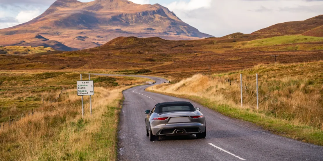 North Coast 500 road trip route through the Scottish Highlands, with a car driving towards the mountains
