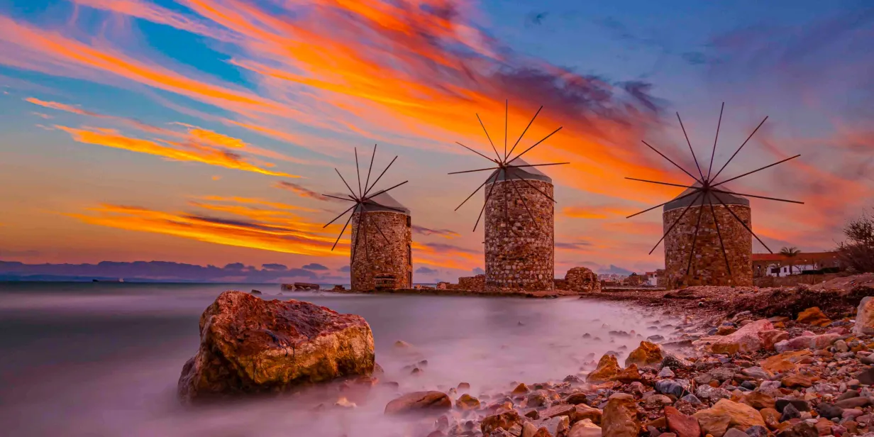 Traditional Greek windmills silhouetted against a vibrant sunset