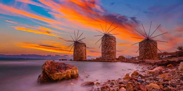 Traditional Greek windmills silhouetted against a vibrant sunset